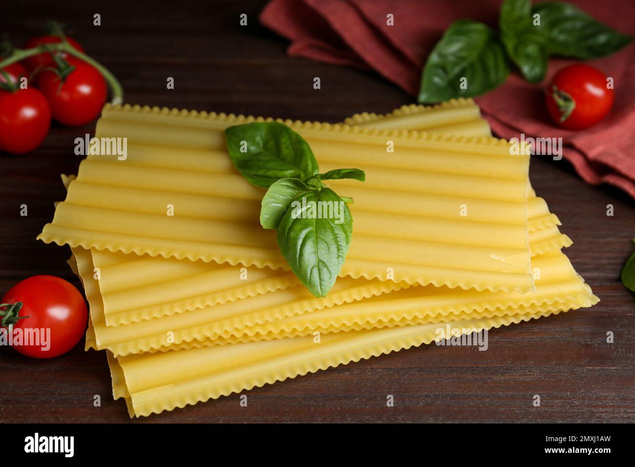 Uncooked lasagna sheets with cherry tomatoes and basil on wooden table ...