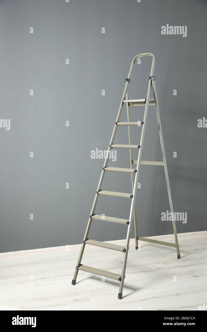 Modern metal step ladder near grey wall Stock Photo - Alamy