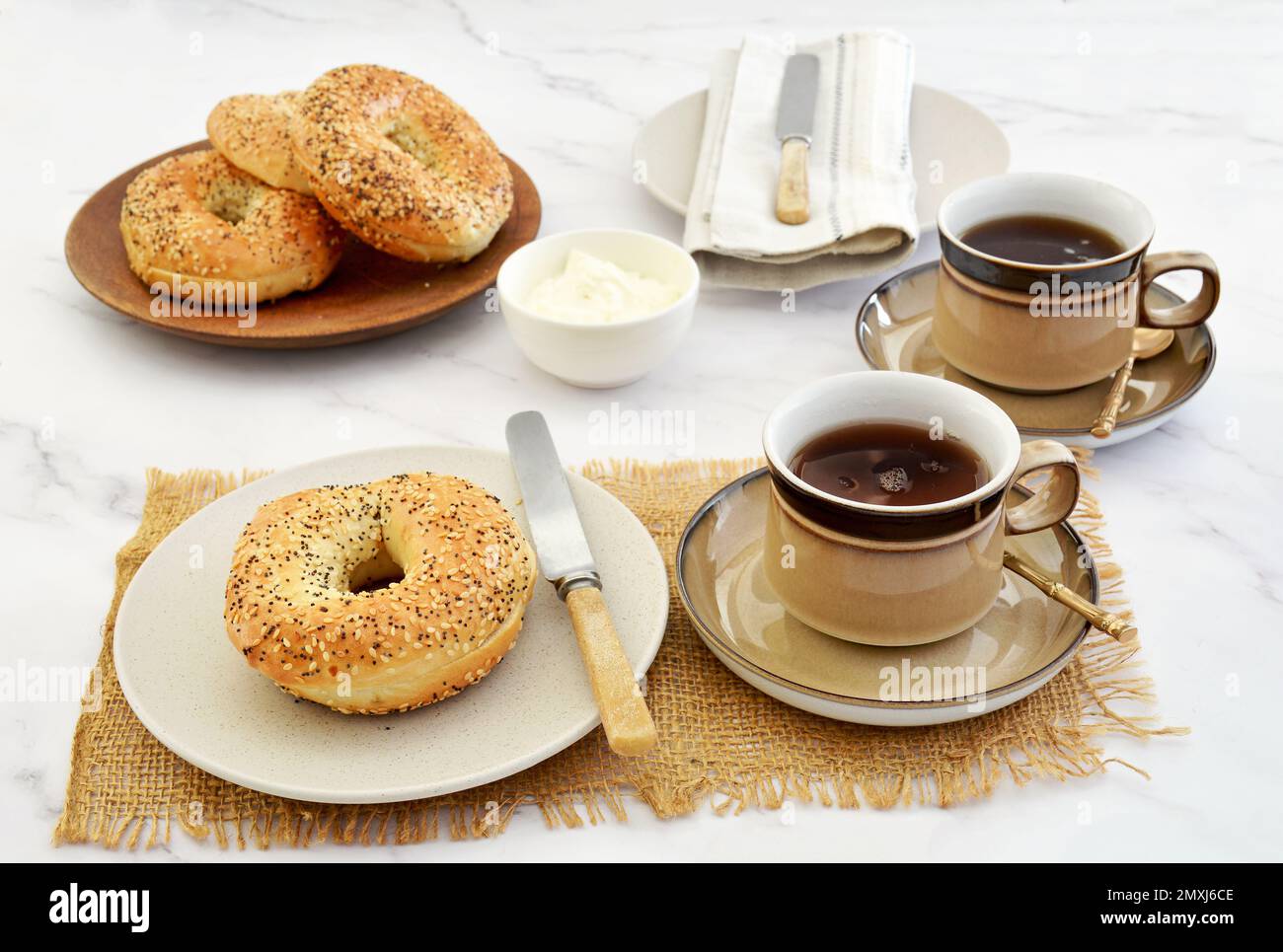 Fresh bagels and cream cheese with cups and saucers for coffee break in ...