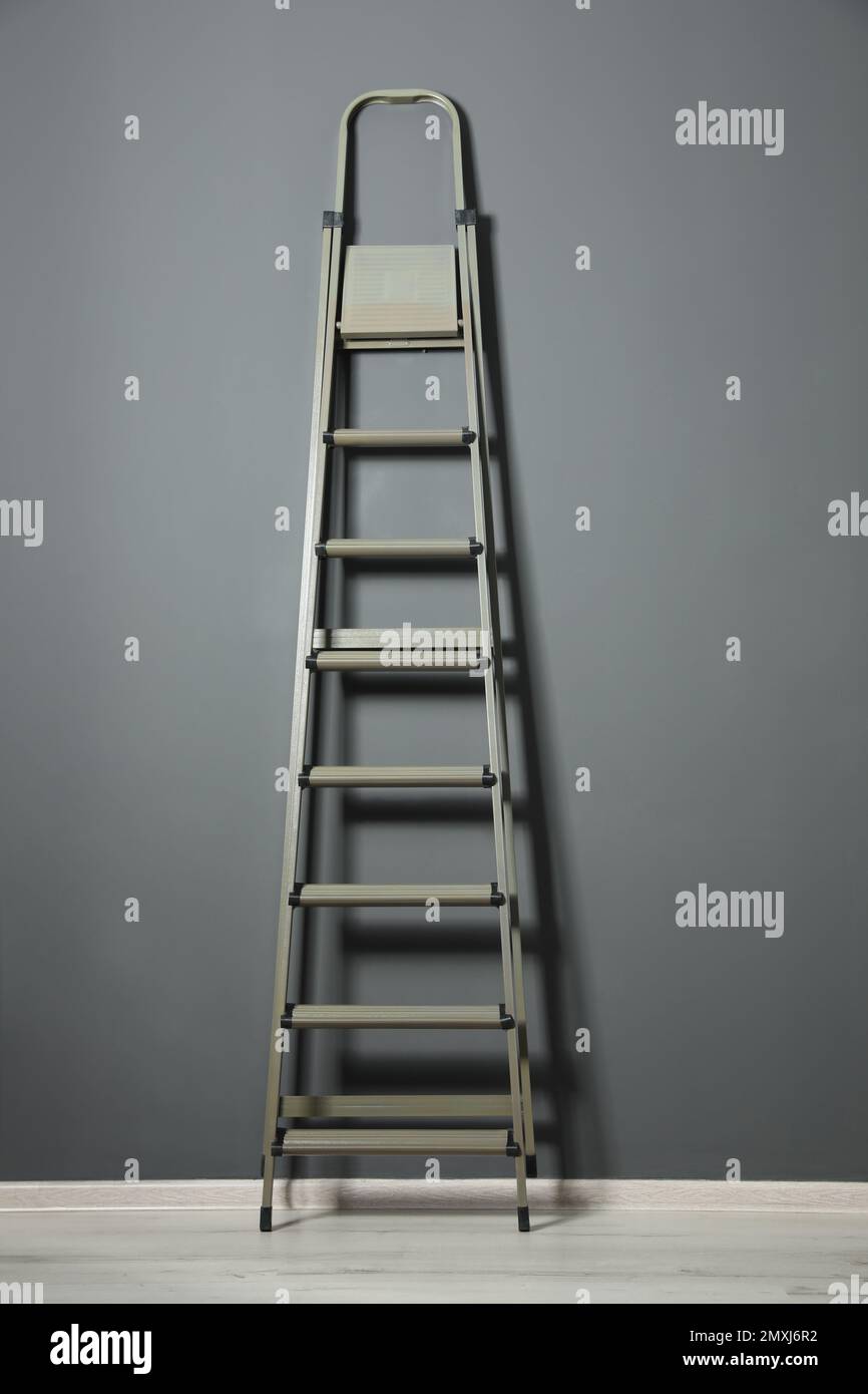 Modern metal step ladder near grey wall Stock Photo - Alamy