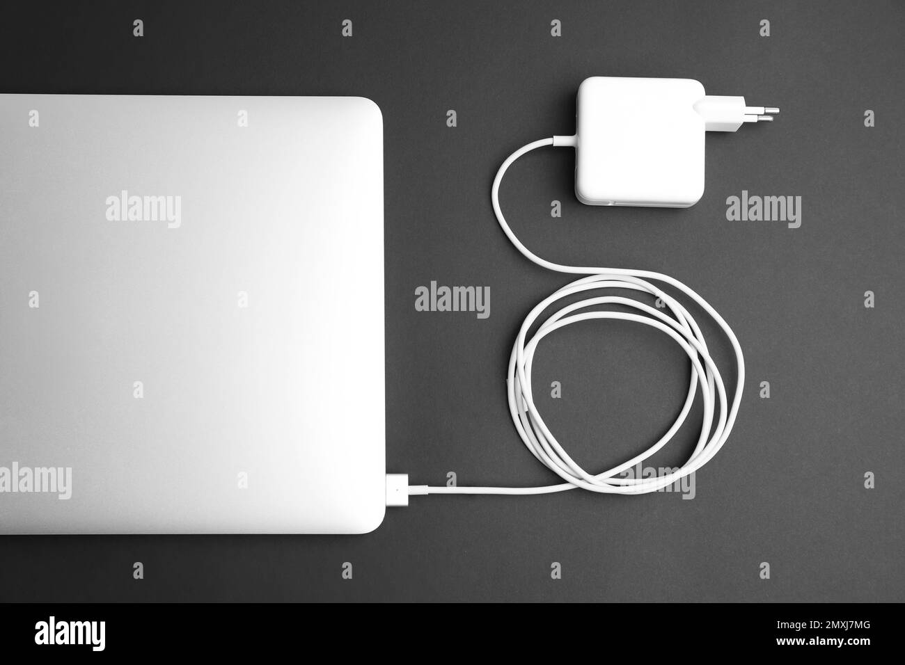 Laptop and charger on black background, flat lay. Modern technology ...
