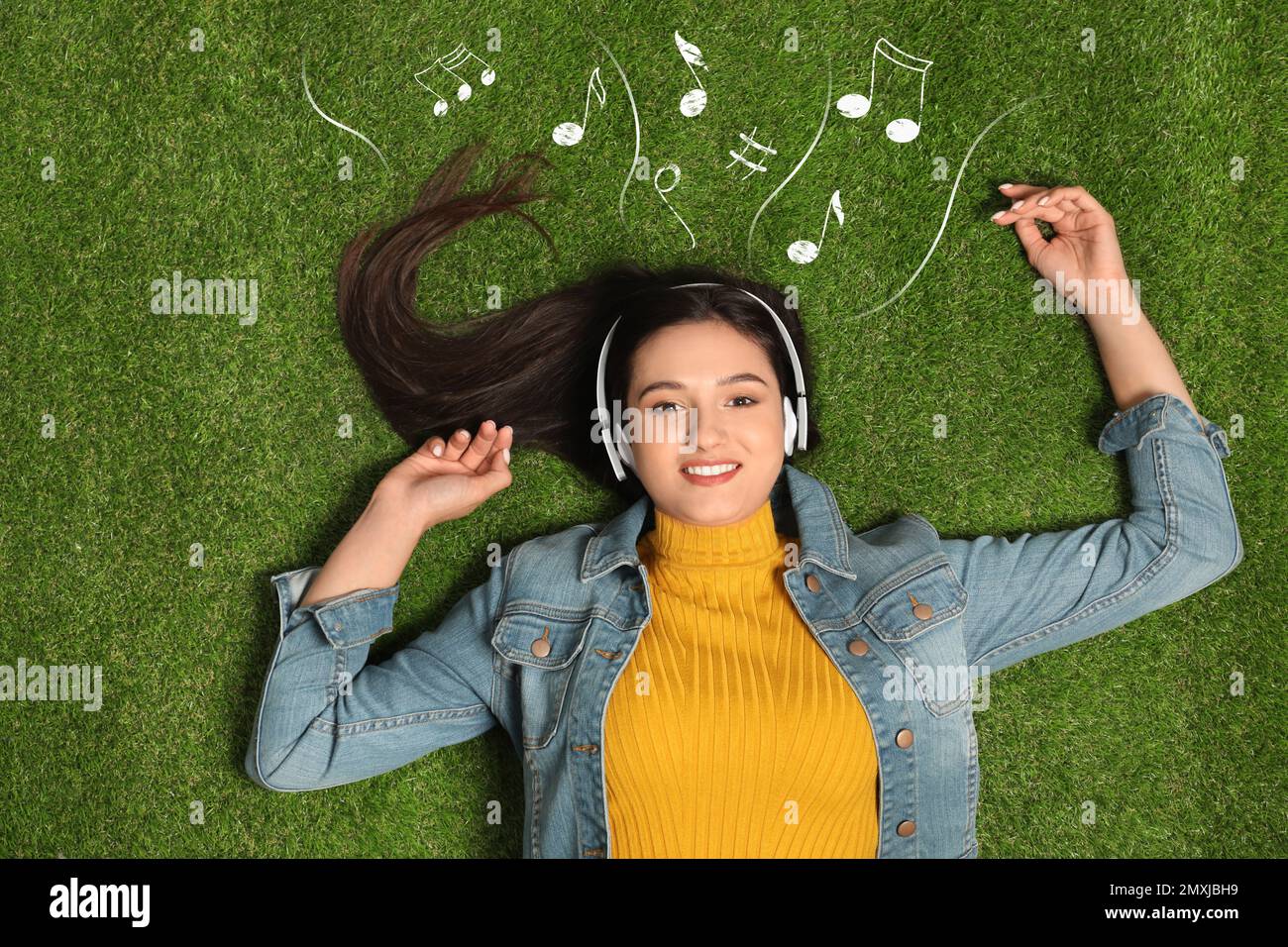 Young woman listening to music through headphones on green grass, top ...