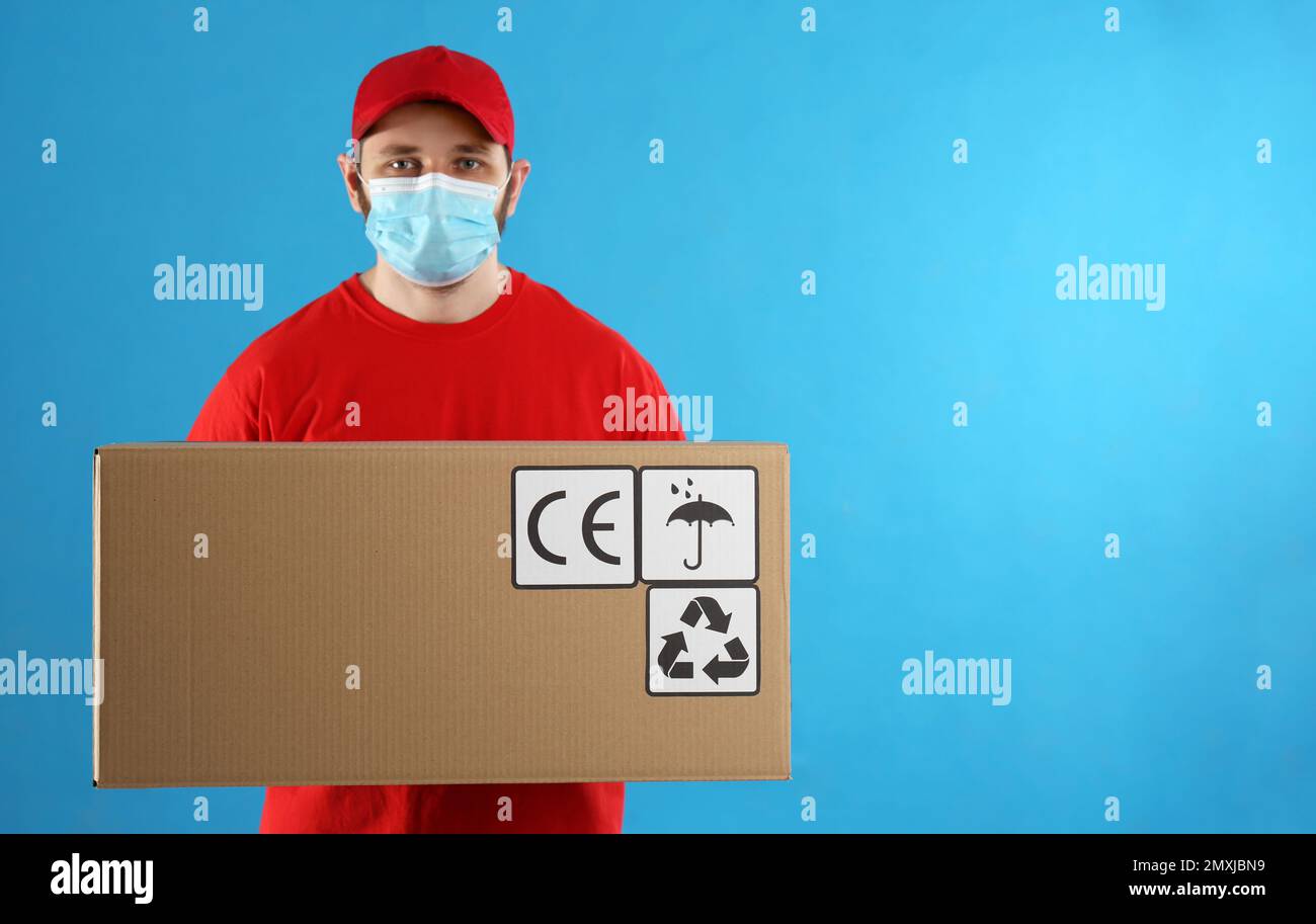 Courier in mask holding cardboard box with different packaging symbols ...