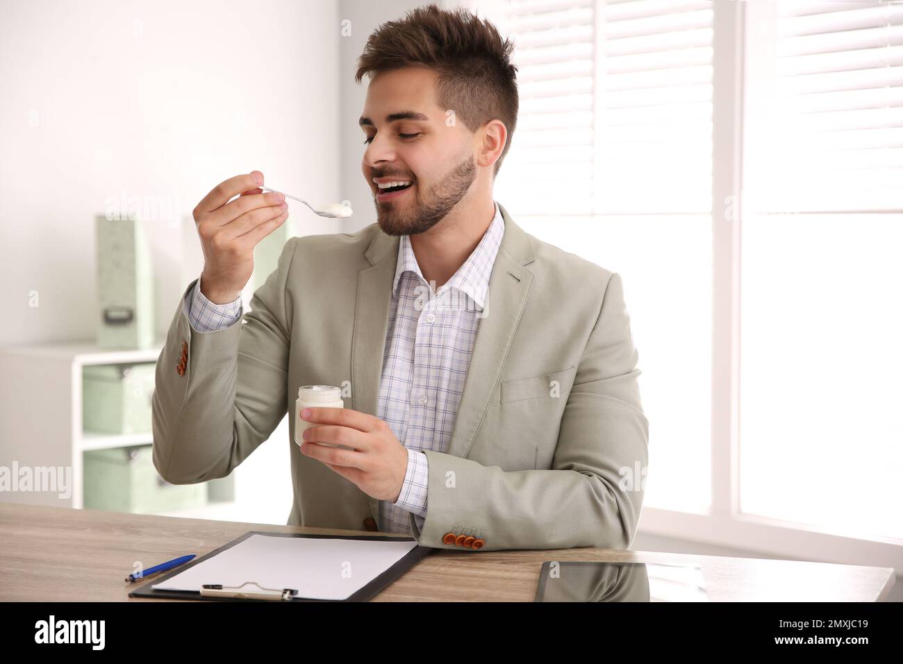 Happy young man eating tasty yogurt in office Stock Photo - Alamy