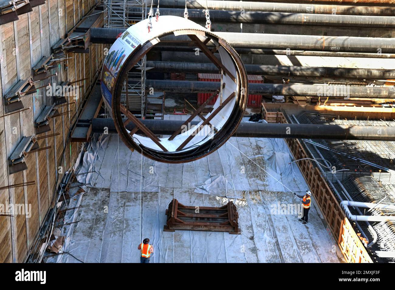Workers lower the tail shield section of a tunnel boring machine into a ...