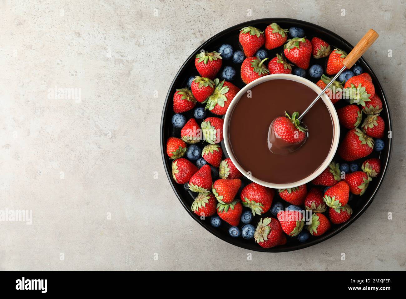 Fondue fork with strawberry in bowl of melted chocolate surrounded by ...