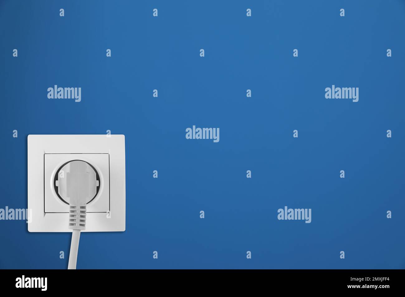 Blue wall with power socket and inserted plug, space for text ...