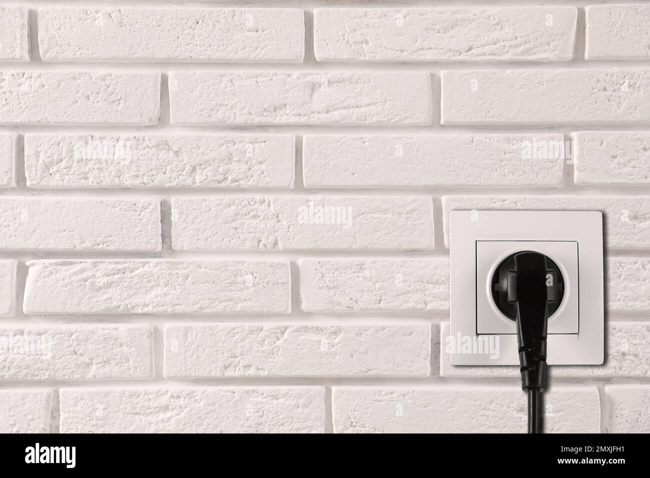 White brick wall with power socket and inserted plug, space for text ...