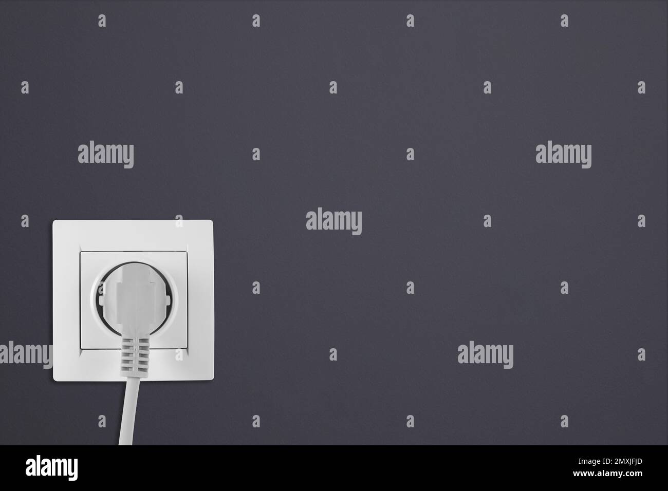Dark grey wall with power socket and inserted plug, space for text ...