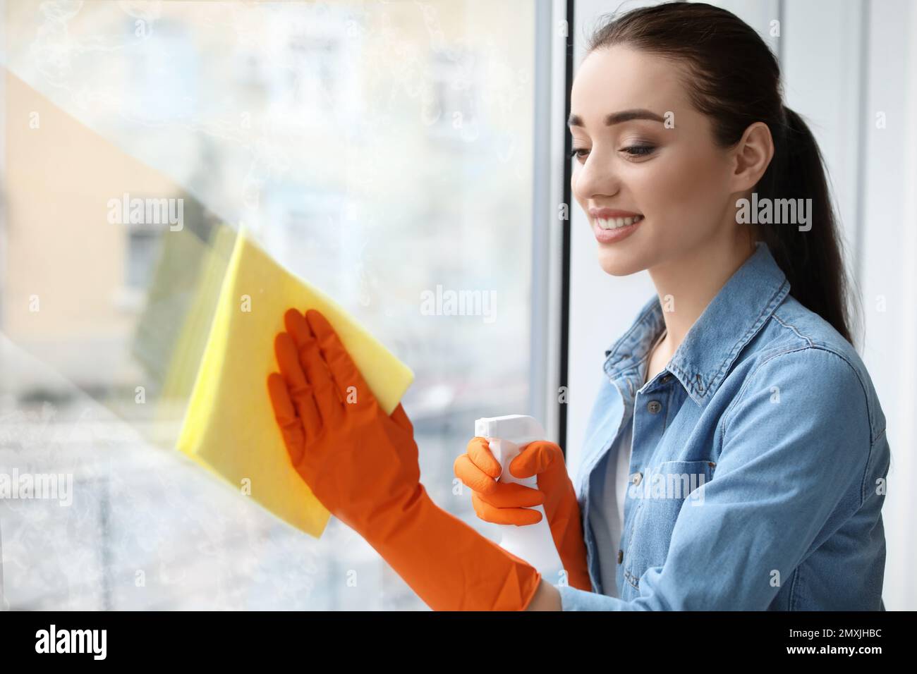Young woman wiping window glass with rag at home. Cleaning service ...