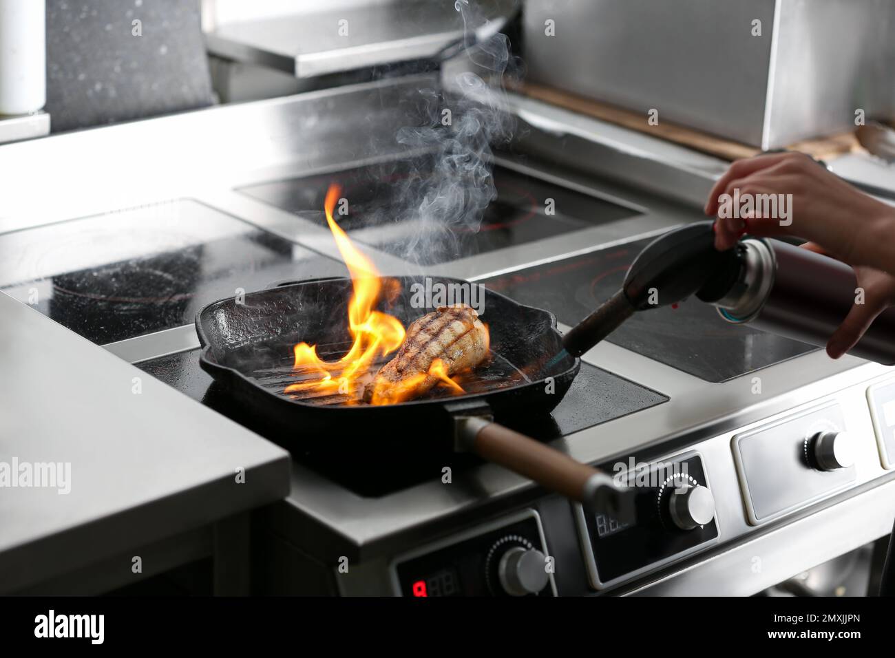 Female chef cooking meat with manual gas burner on stove in restaurant ...