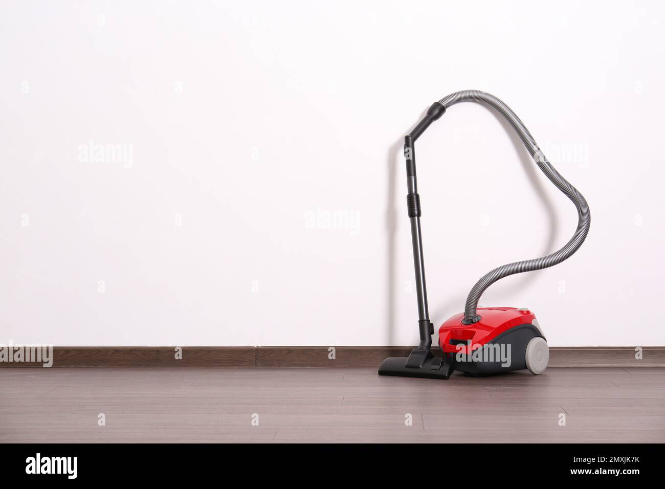 Modern red vacuum cleaner on wooden floor near white wall, space for ...