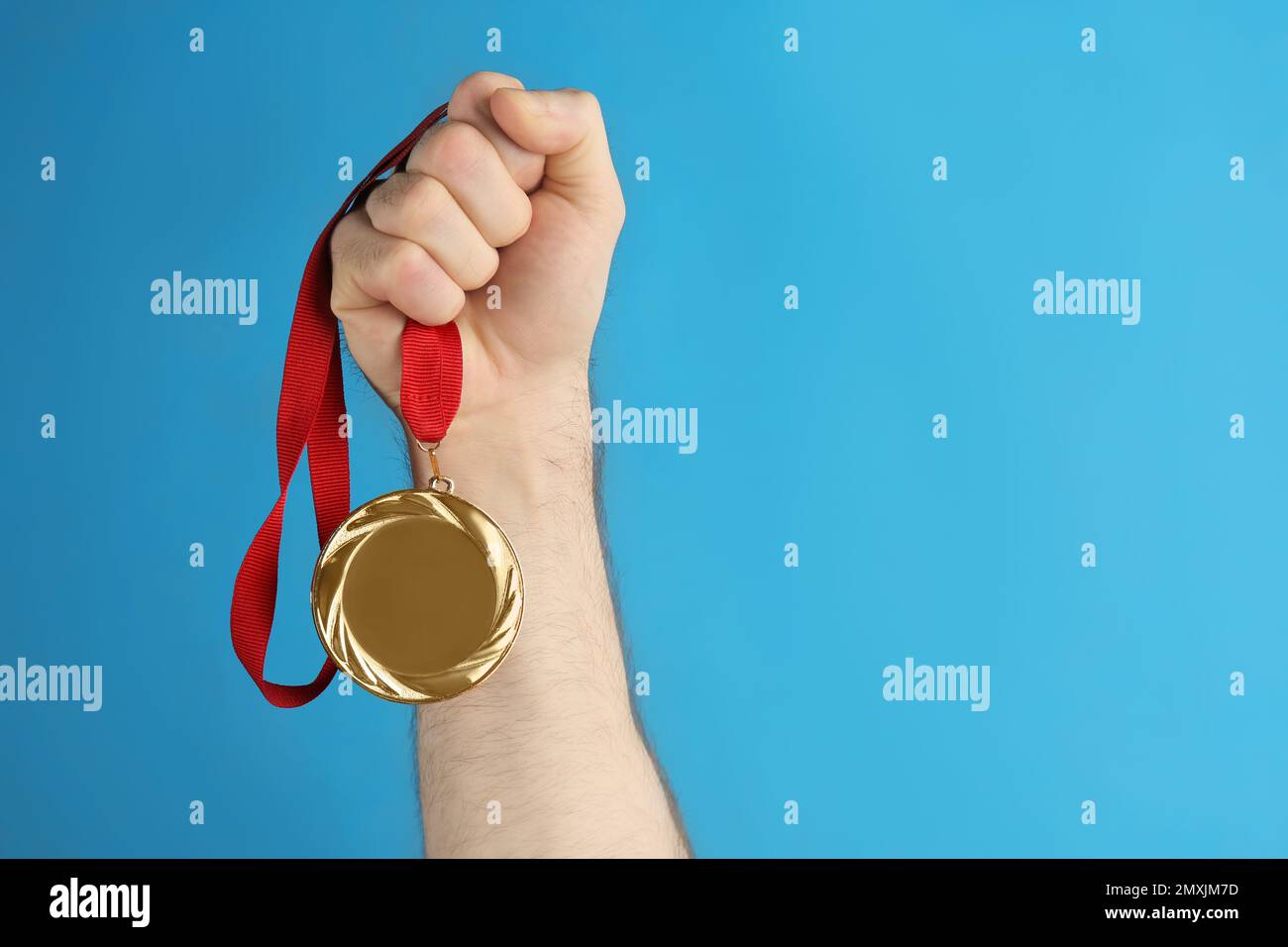 Man holding golden medal on blue background, closeup. Space for design ...