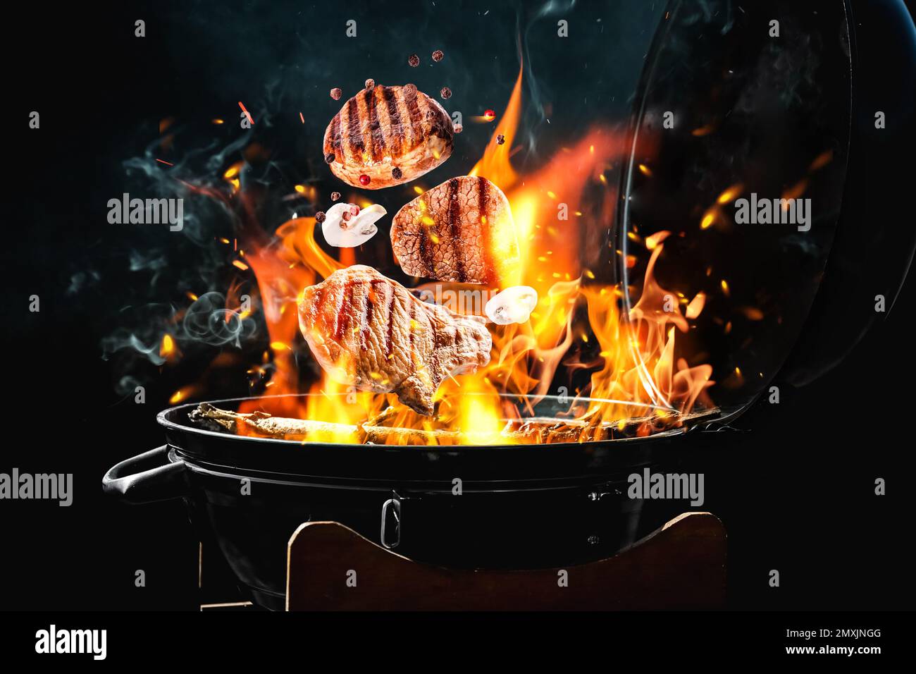 Meat and mushrooms falling onto barbecue grill with flame against black ...