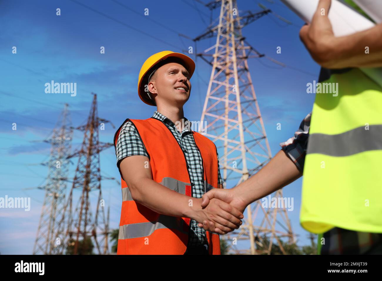 Professional electricians shaking hands near high voltage tower ...