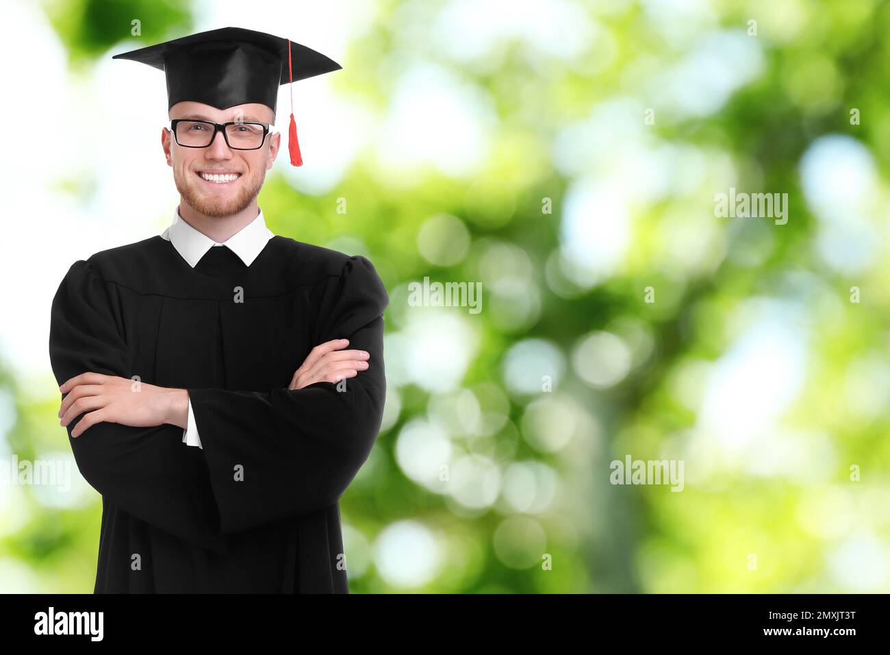 Happy student wearing graduation hat on blurred background, space for ...