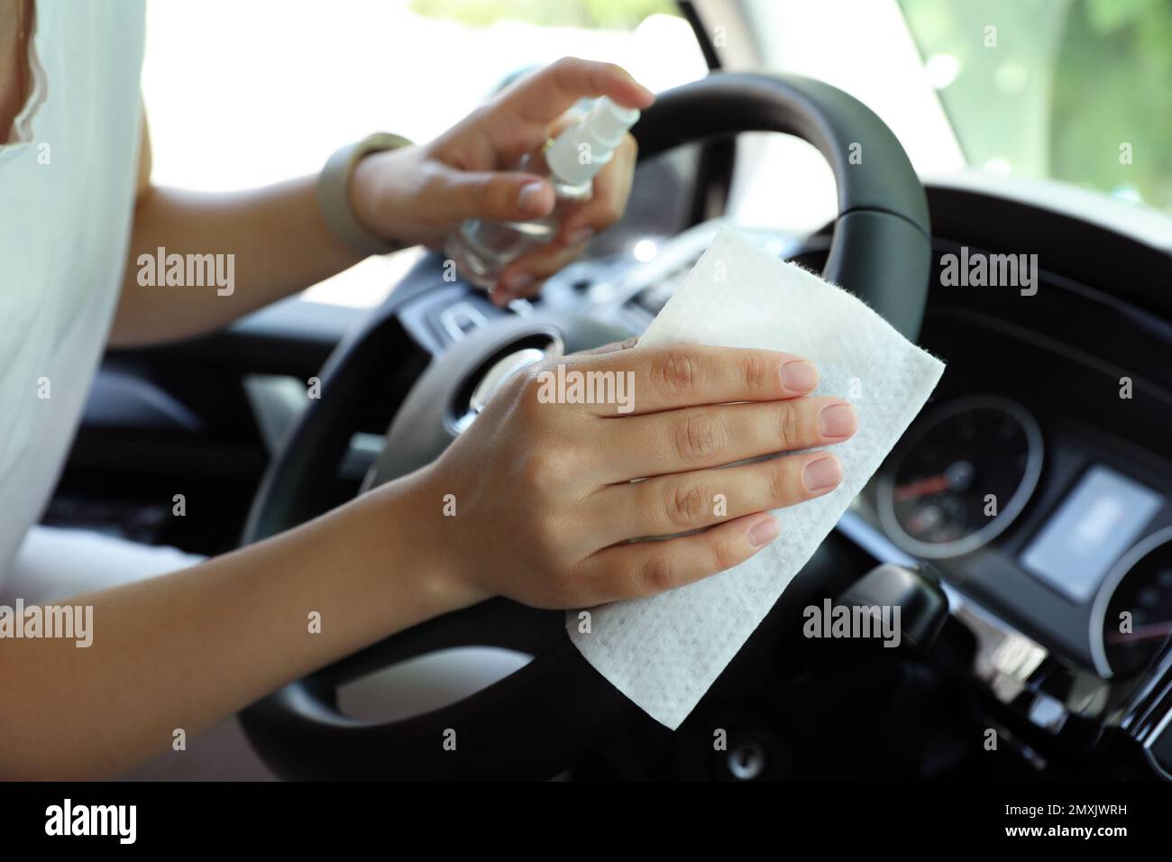 Woman cleaning steering wheel with wet wipe and antibacterial spray in ...