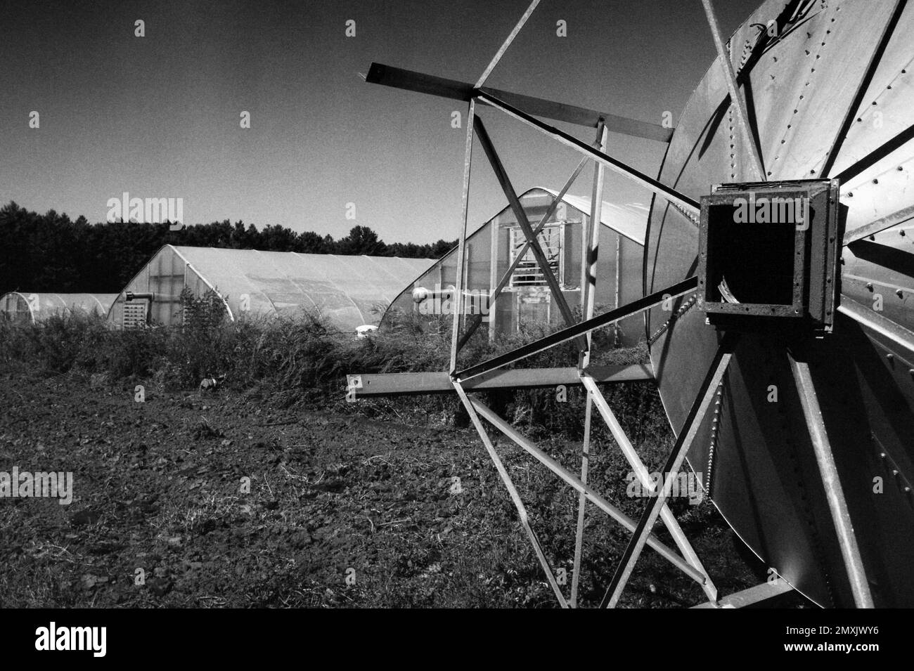 A fallen metal silo rests on the grass with a row of greenhouses in the ...