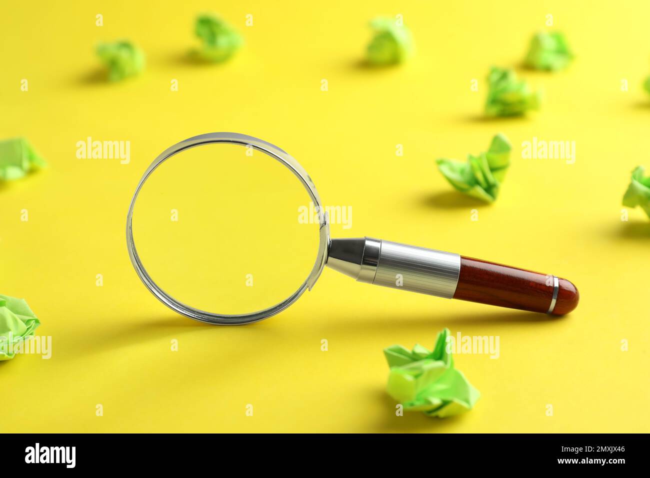 Magnifier glass and green crumpled paper sheets on yellow background ...