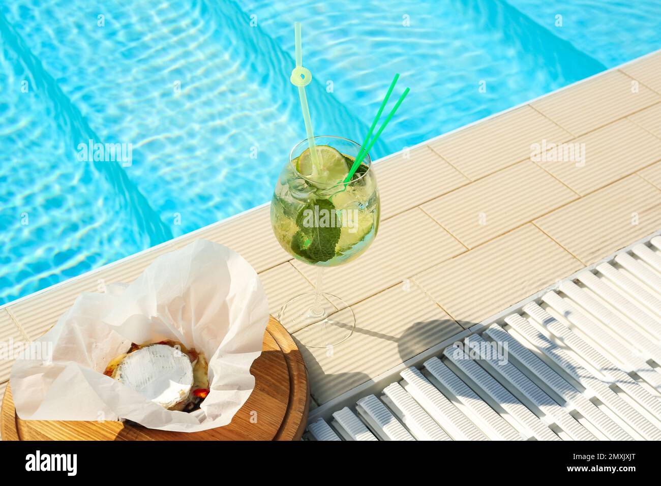 Glass of delicious mojito and brie cheese near swimming pool ...
