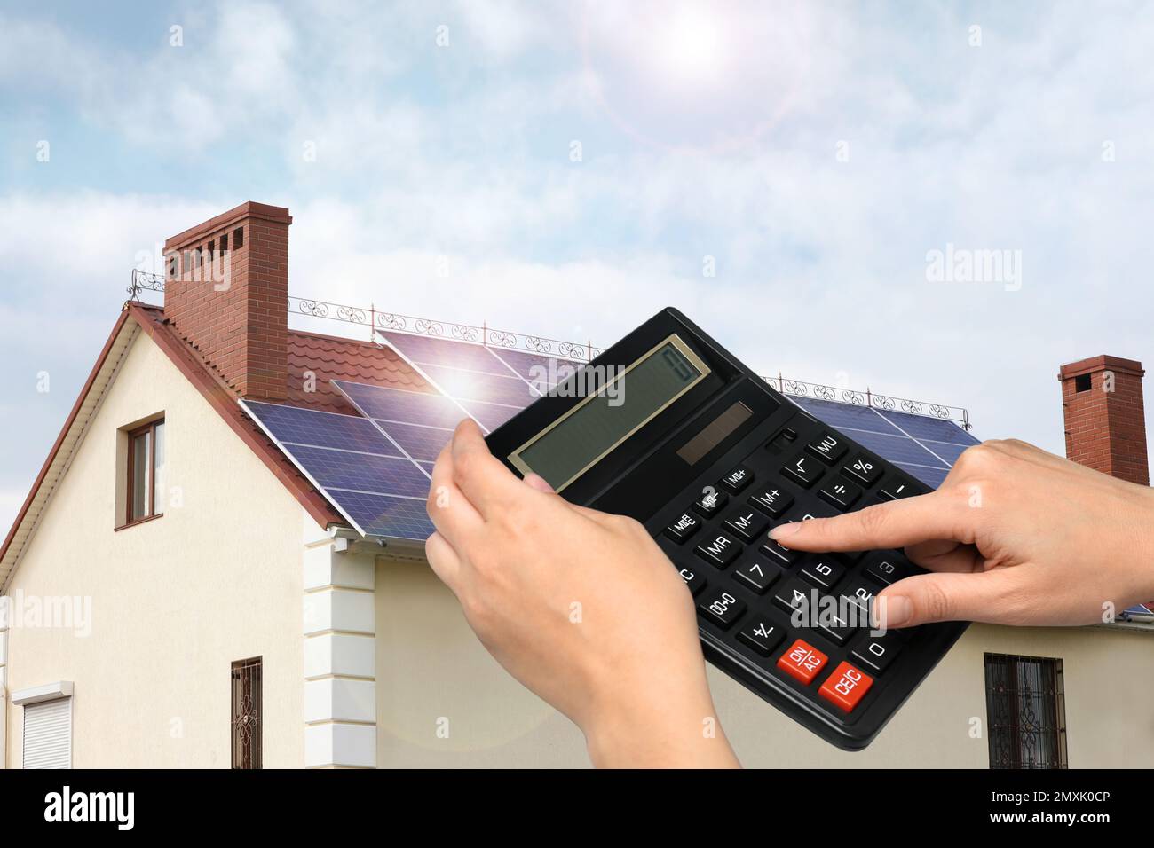 Woman using calculator against house with installed solar panels ...