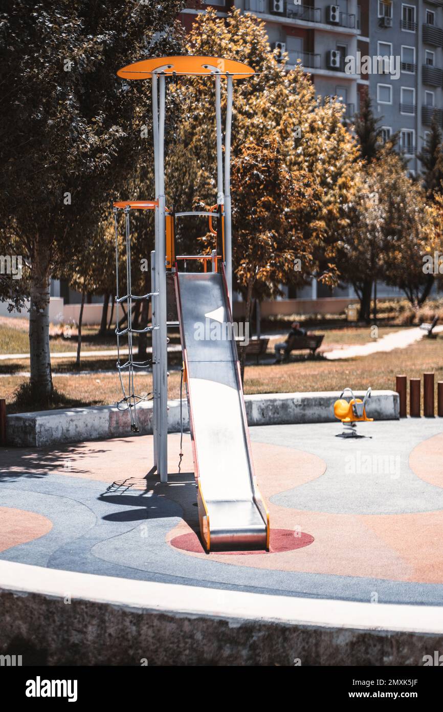 Vertical capture on a playground surrounded by trees, a narrow swing ...