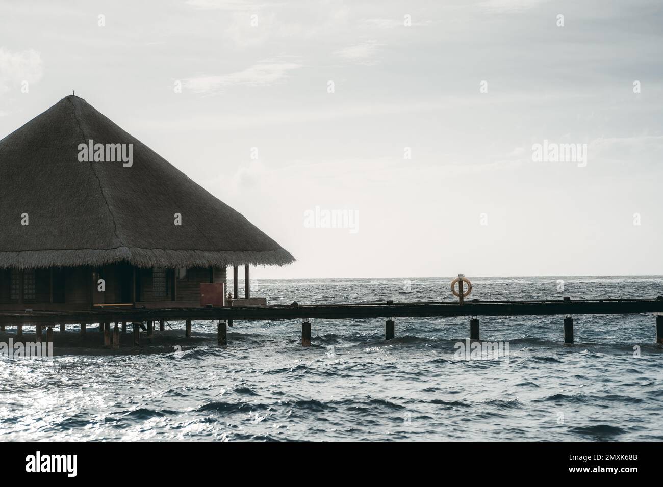 A close-up of an overwater bungalow, with a thatched roof, connected to ...