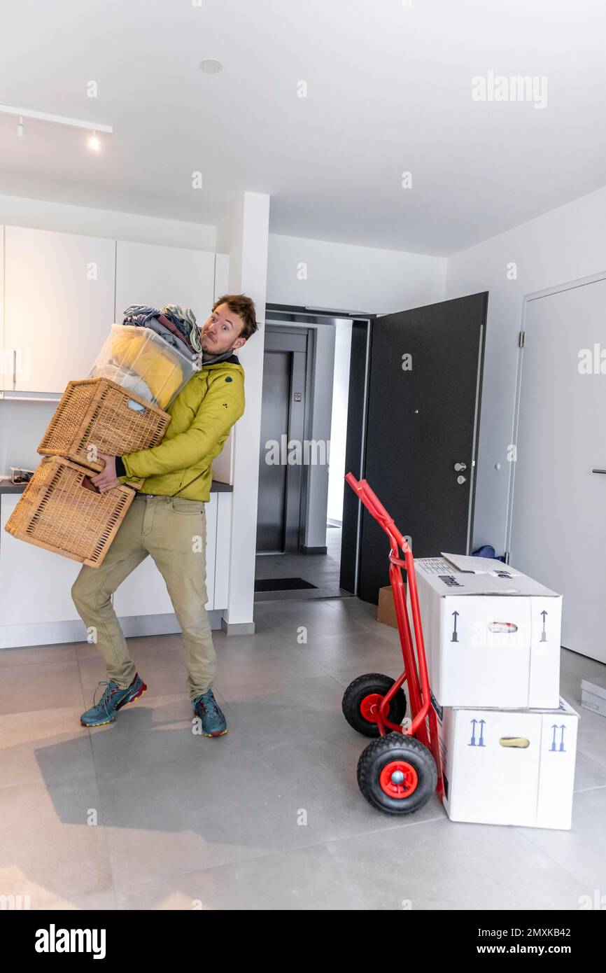 Young man carrying heavy moving boxes, standing in modern kitchen of a ...