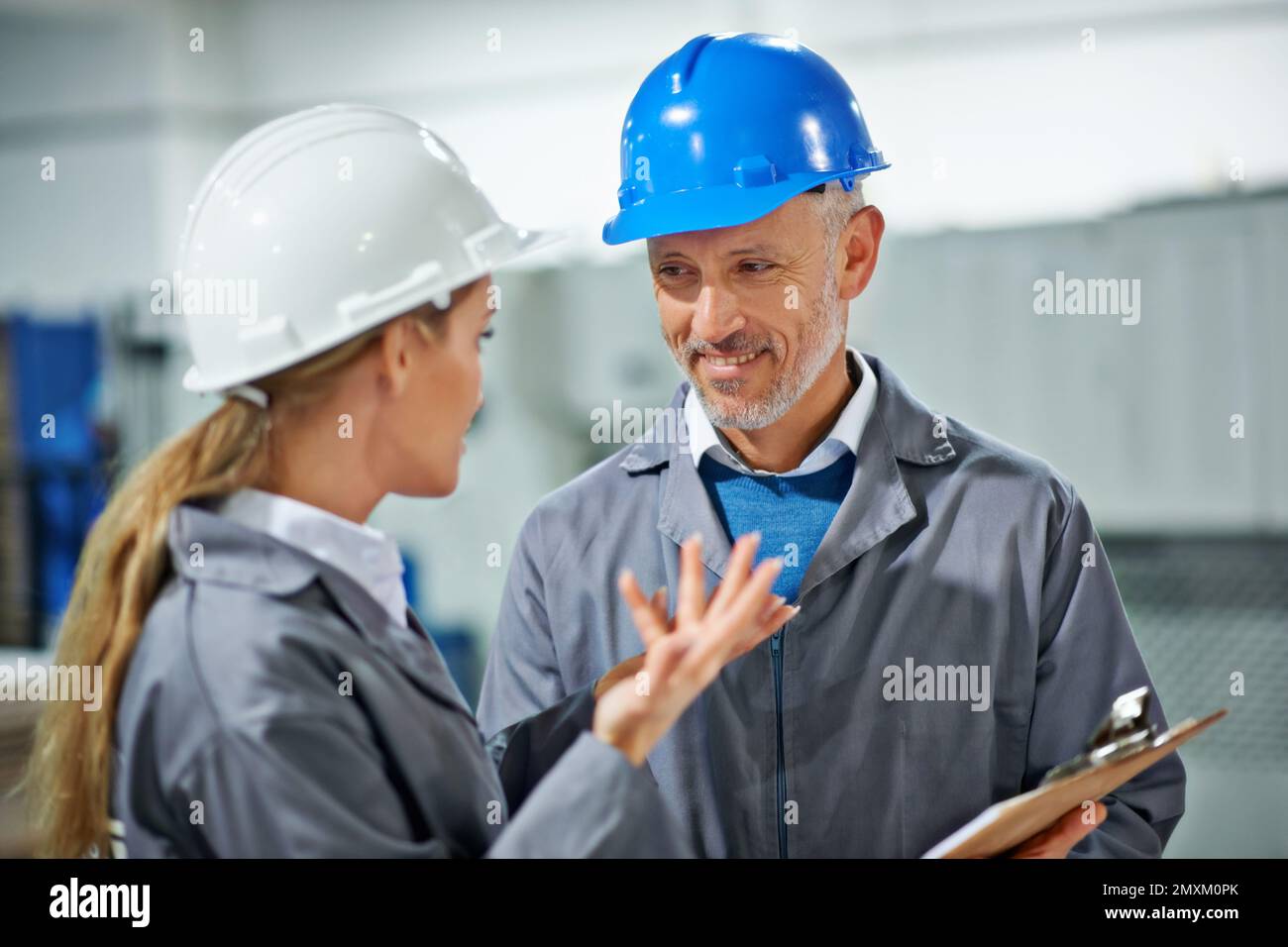 Creating good work relationships. Two factory employees wearing hardhats having a discussion ...