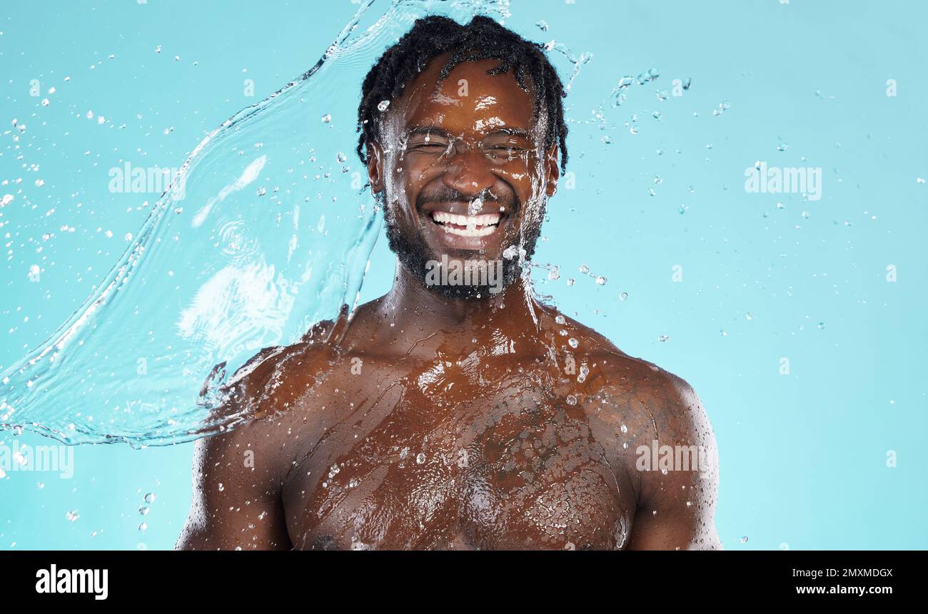Water splash, beauty and black man isolated on blue background for face cleaning, body shower ...