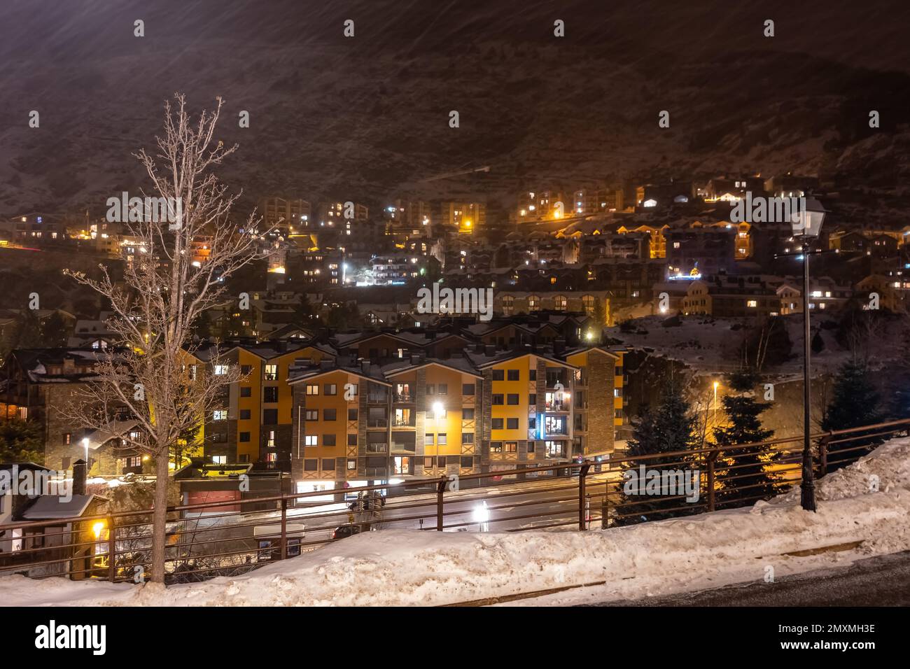 Urbanization of mountain houses at night with lights on while it snows ...
