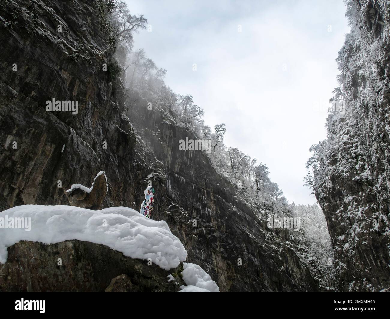 A sacred small column with colored ribbons in a gorge covered with snow ...