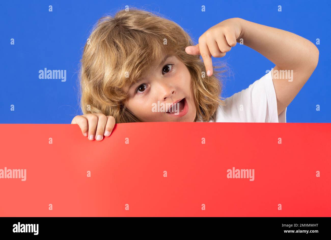 Excited child pointing on blank banner on studio background ...