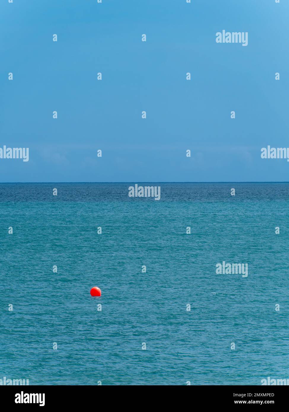 Clear blue sky over a blue sea. An orange buoy on the surface of the ...