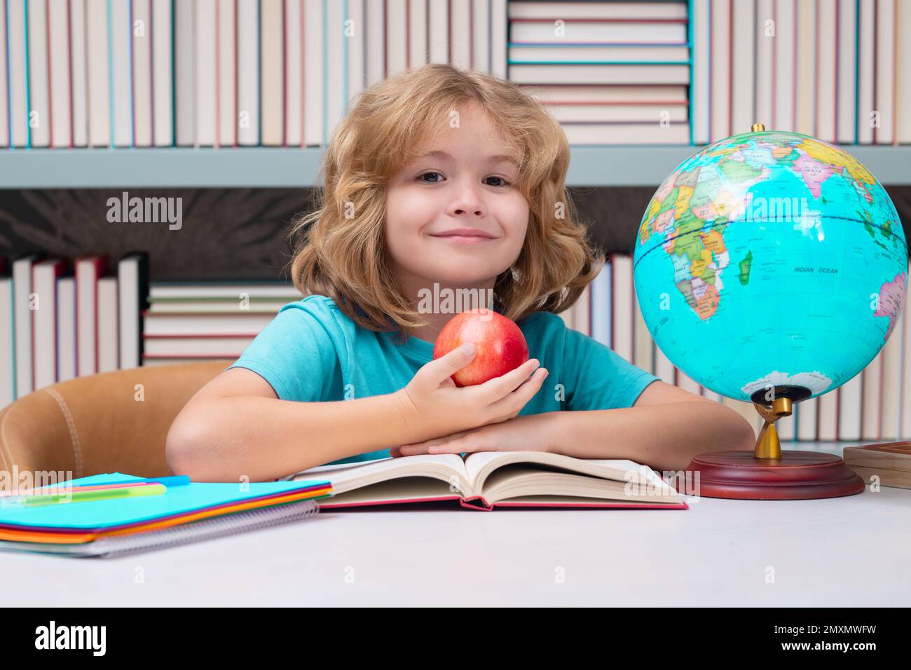 School boy with books and apple in library. School child studying in ...