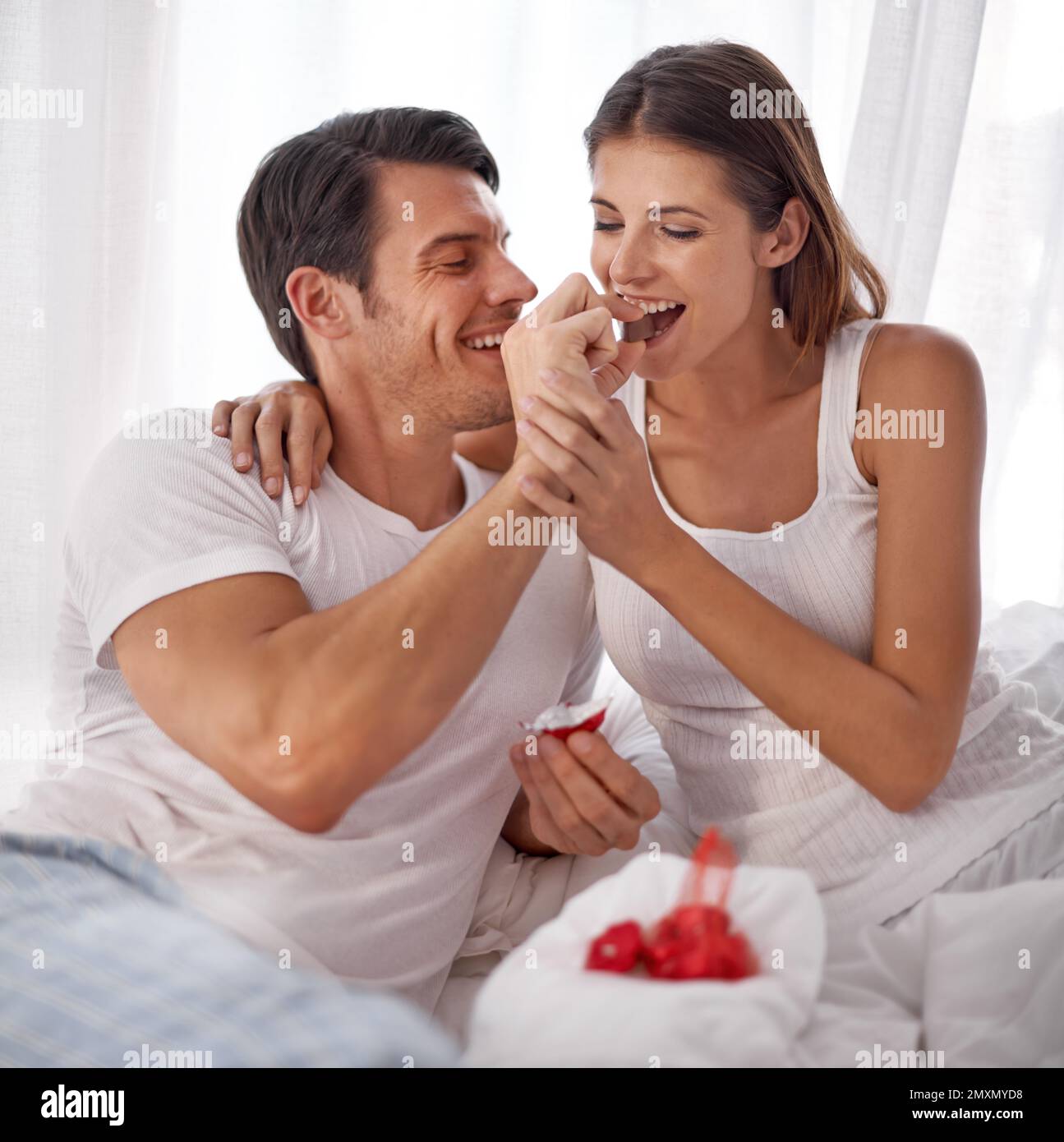 Love, man feeding chocolate to woman and in bed with happiness ...