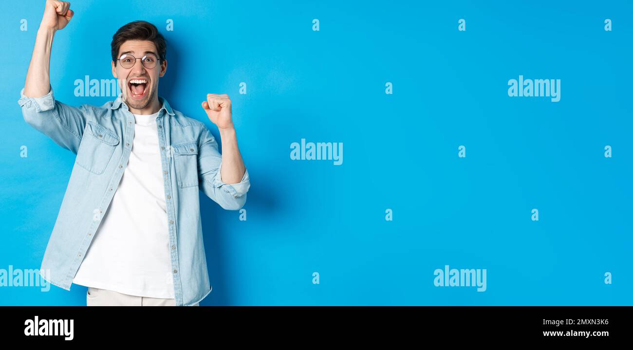 Excited handsome man triumphing, raising hands up and shouting for joy ...