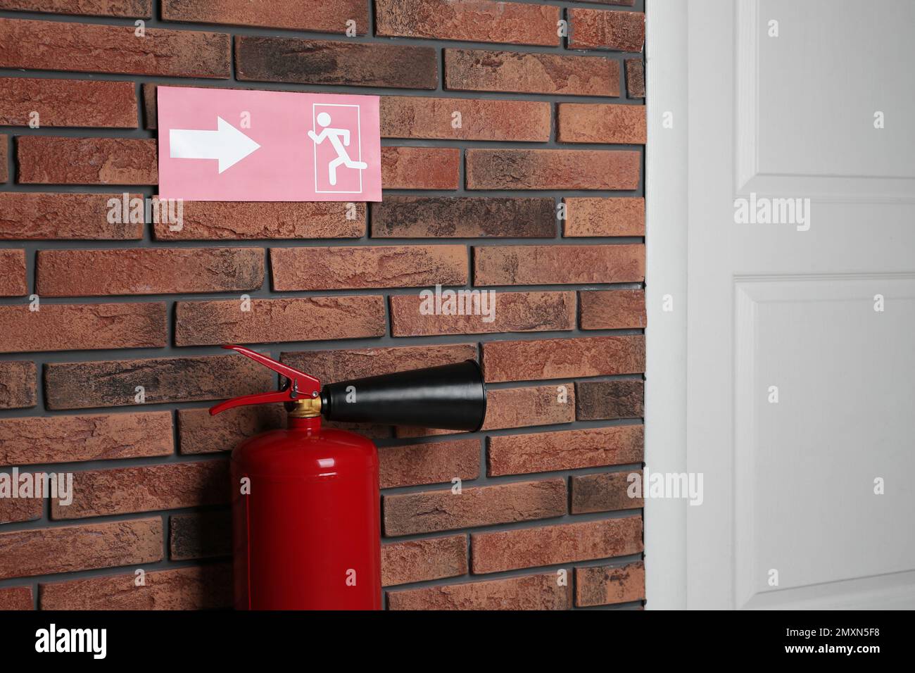 Fire extinguisher and emergency exit sign on brick wall indoors Stock ...