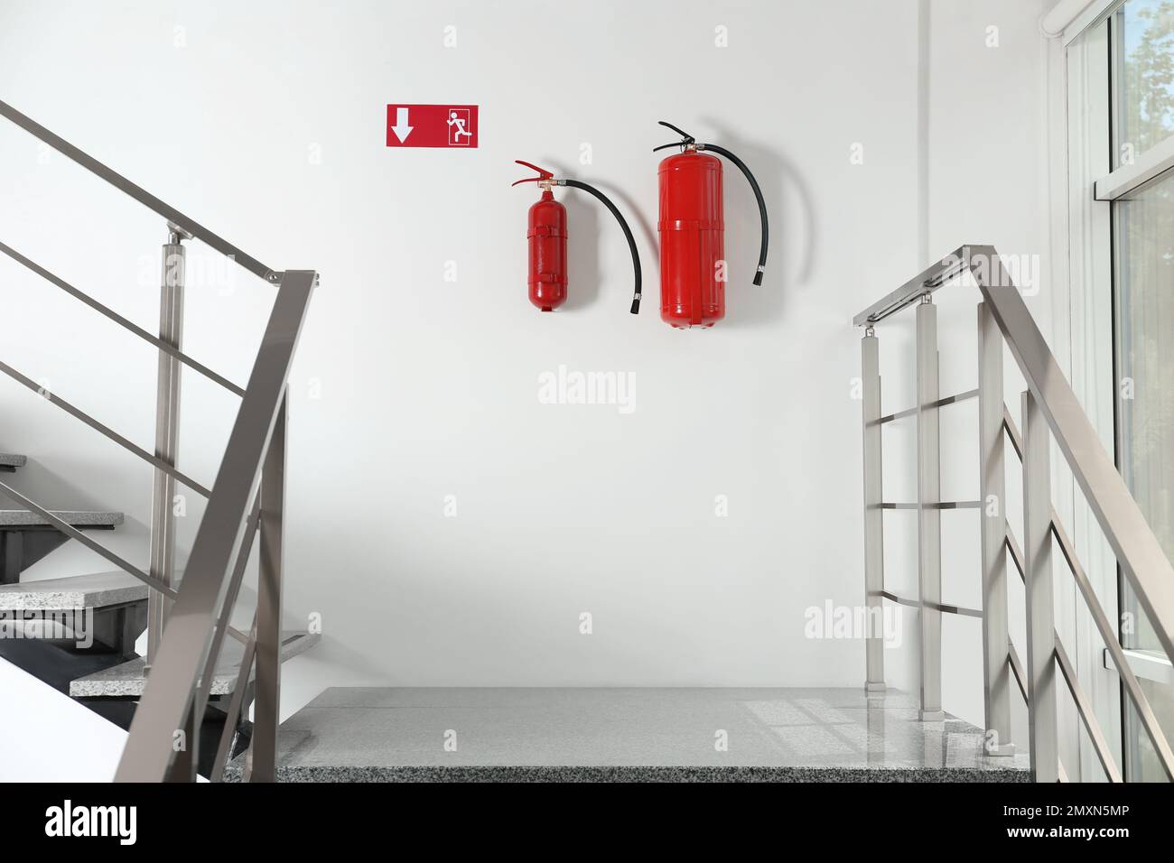 Fire extinguishers and emergency exit sign on white wall near staircase ...