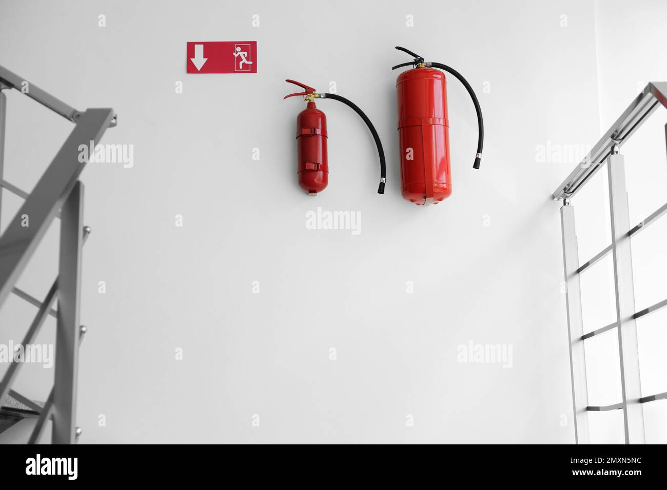 Fire extinguishers and emergency exit sign on white wall near staircase ...