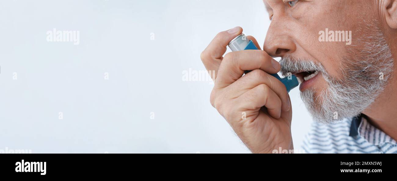 Closeup view of man using asthma inhaler on white background, space for ...