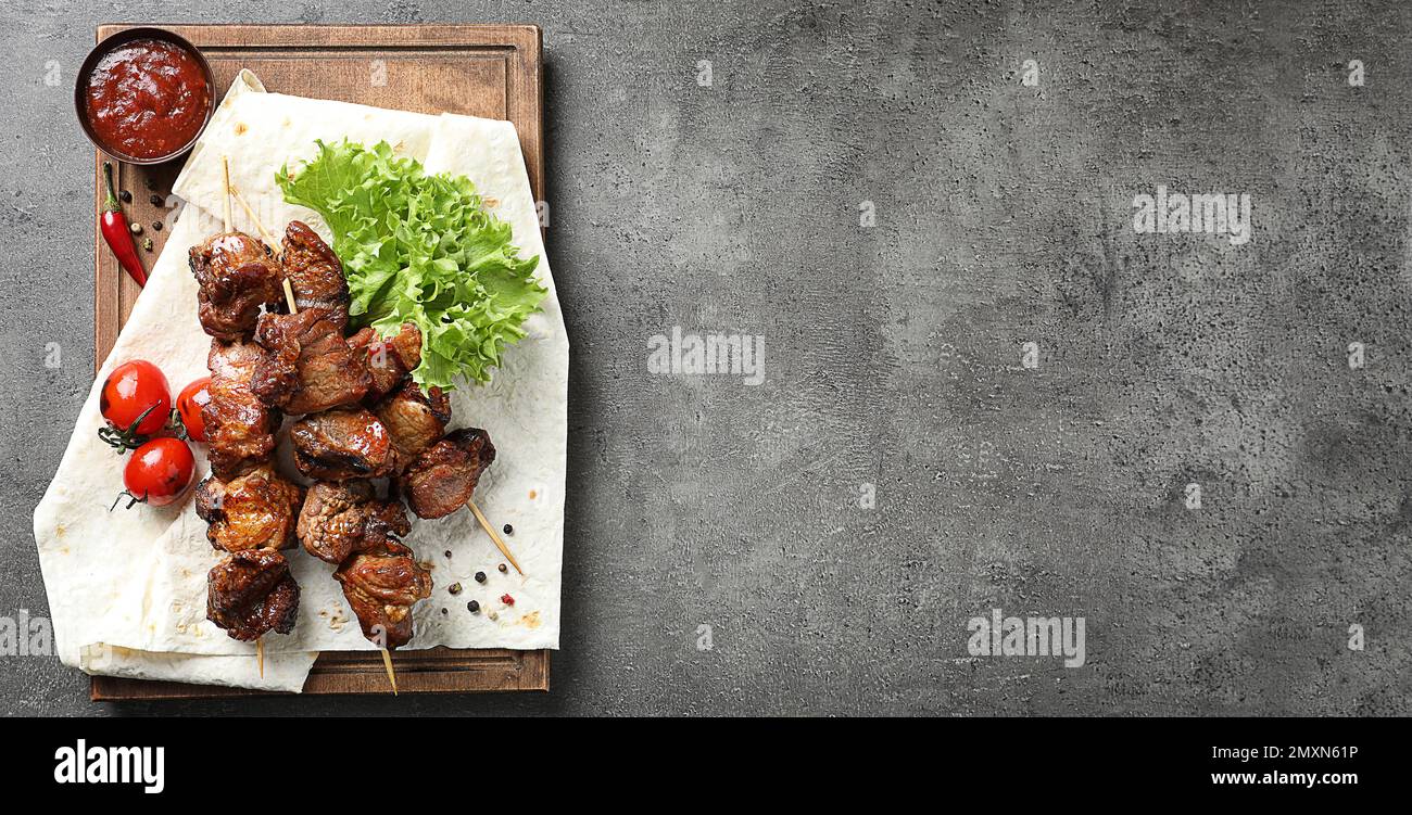 Wooden board with delicious barbecued meat and space for text on gray ...