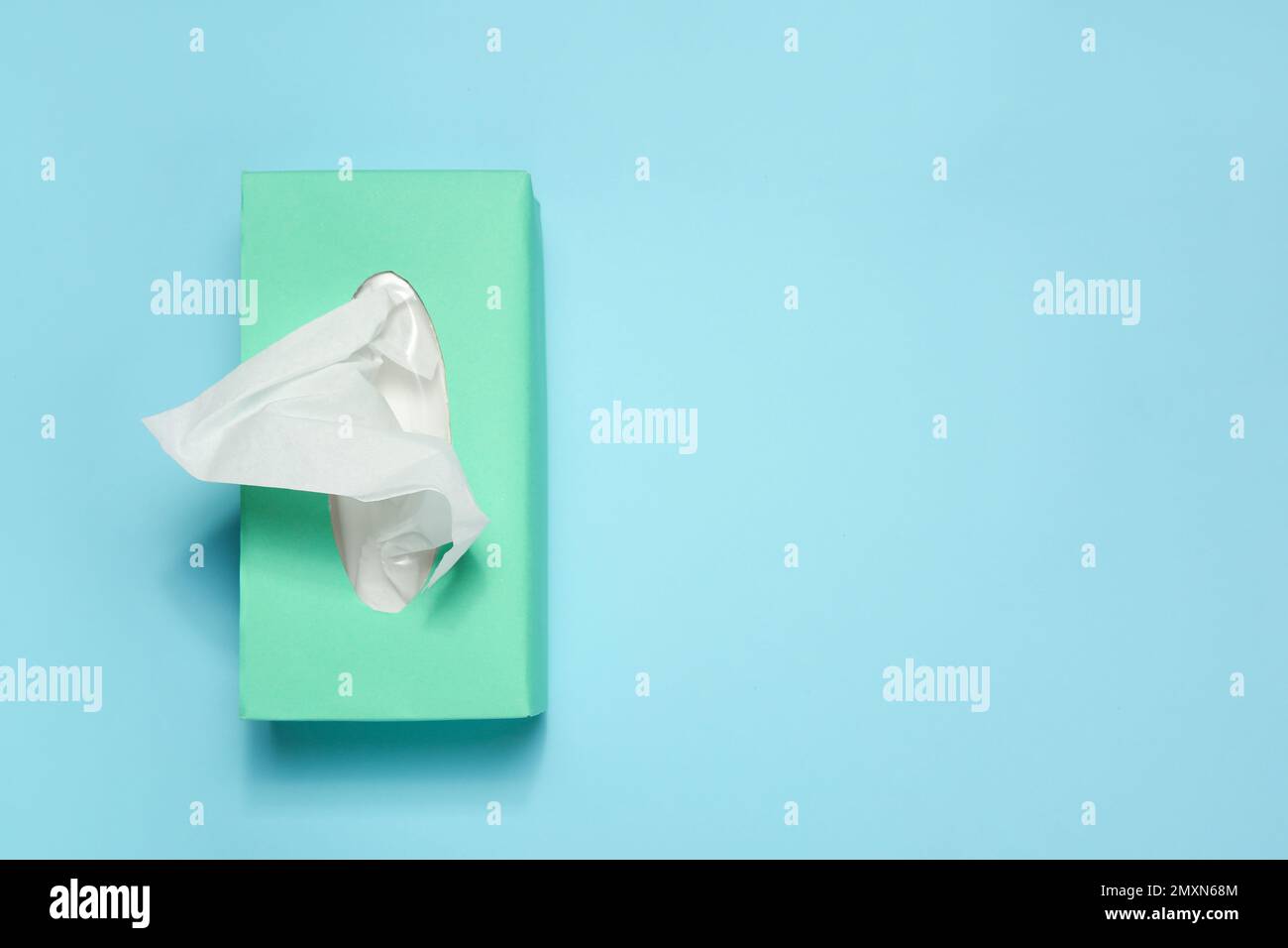 Box with paper tissues on light blue background, top view. Space for ...