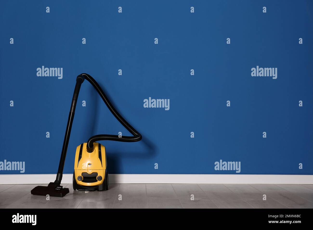 Modern yellow vacuum cleaner on floor near blue wall, space for text ...