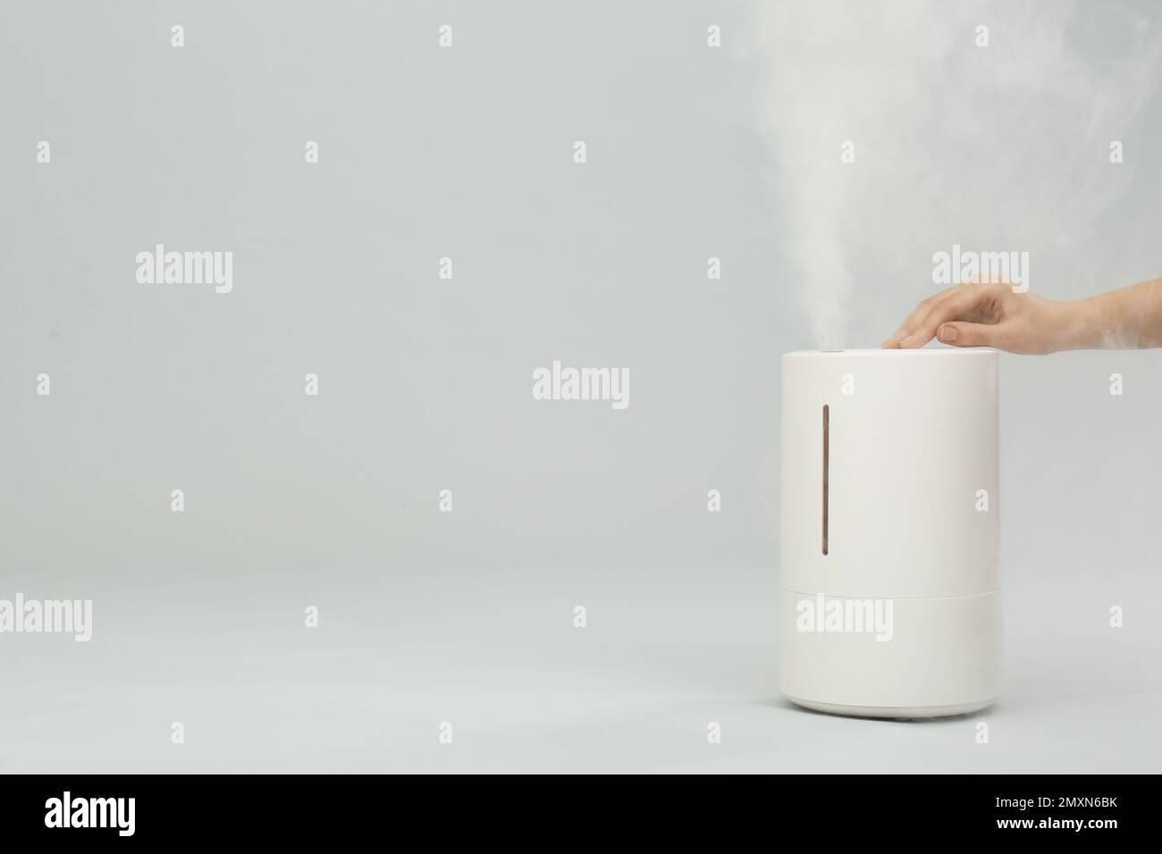 Woman using modern air humidifier on light grey background, closeup ...