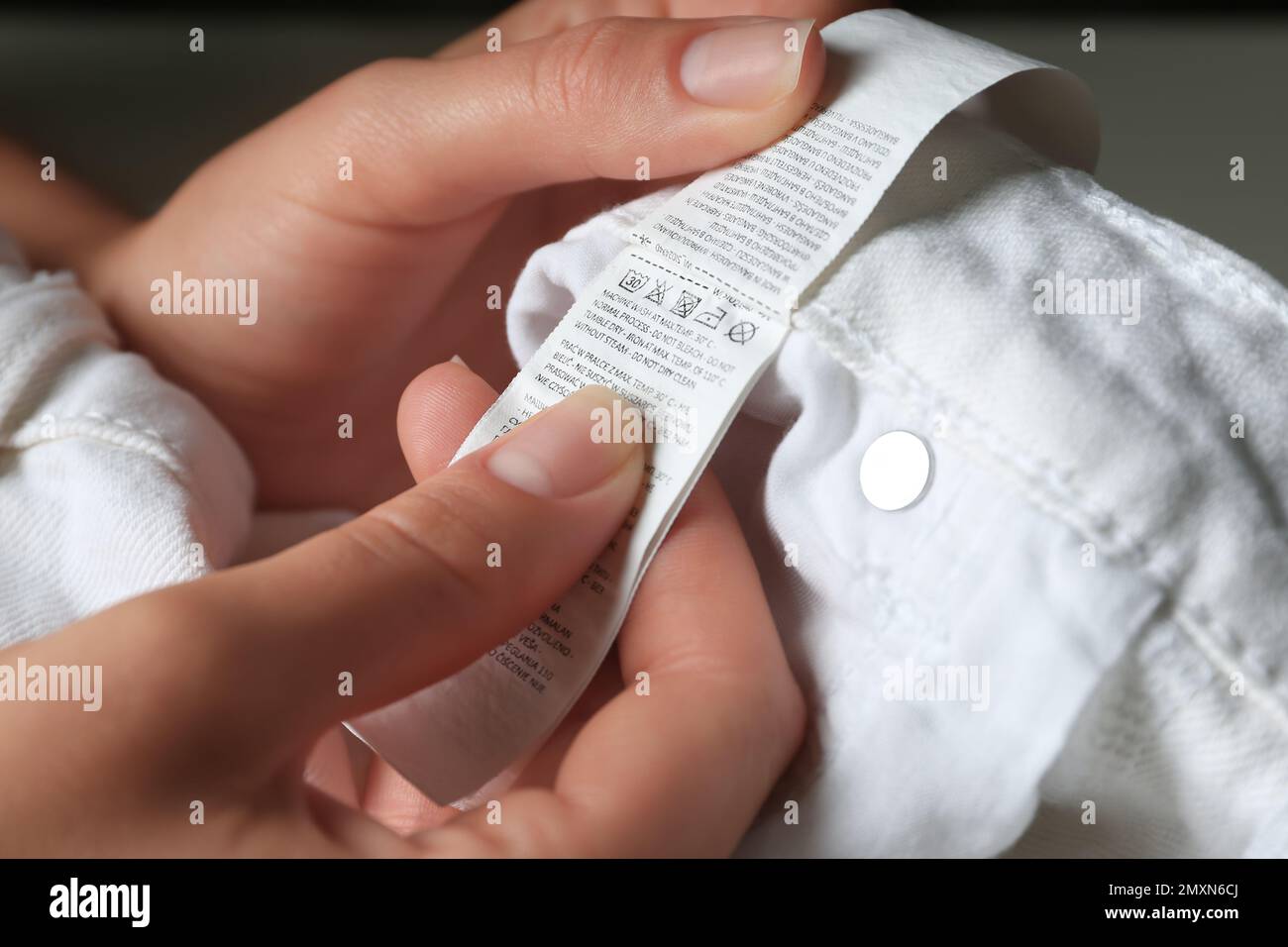 Woman reading clothing label with care instructions on white garment ...