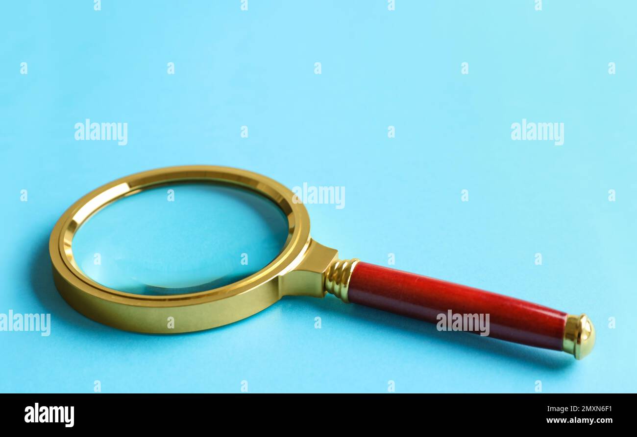 Closeup view of magnifier glass on light blue background, space for ...