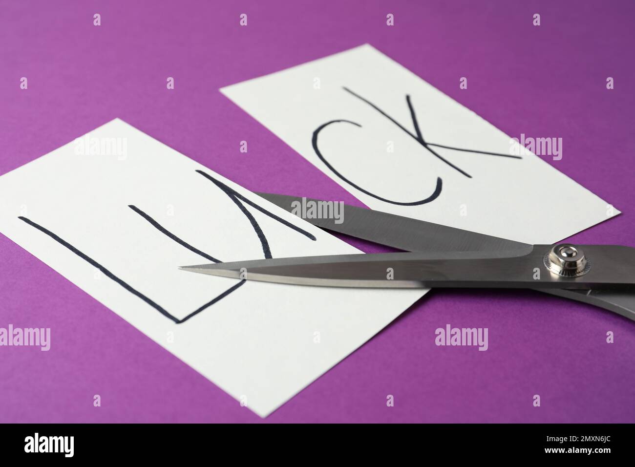 Cut paper with word LUCK and scissors on purple background, closeup ...