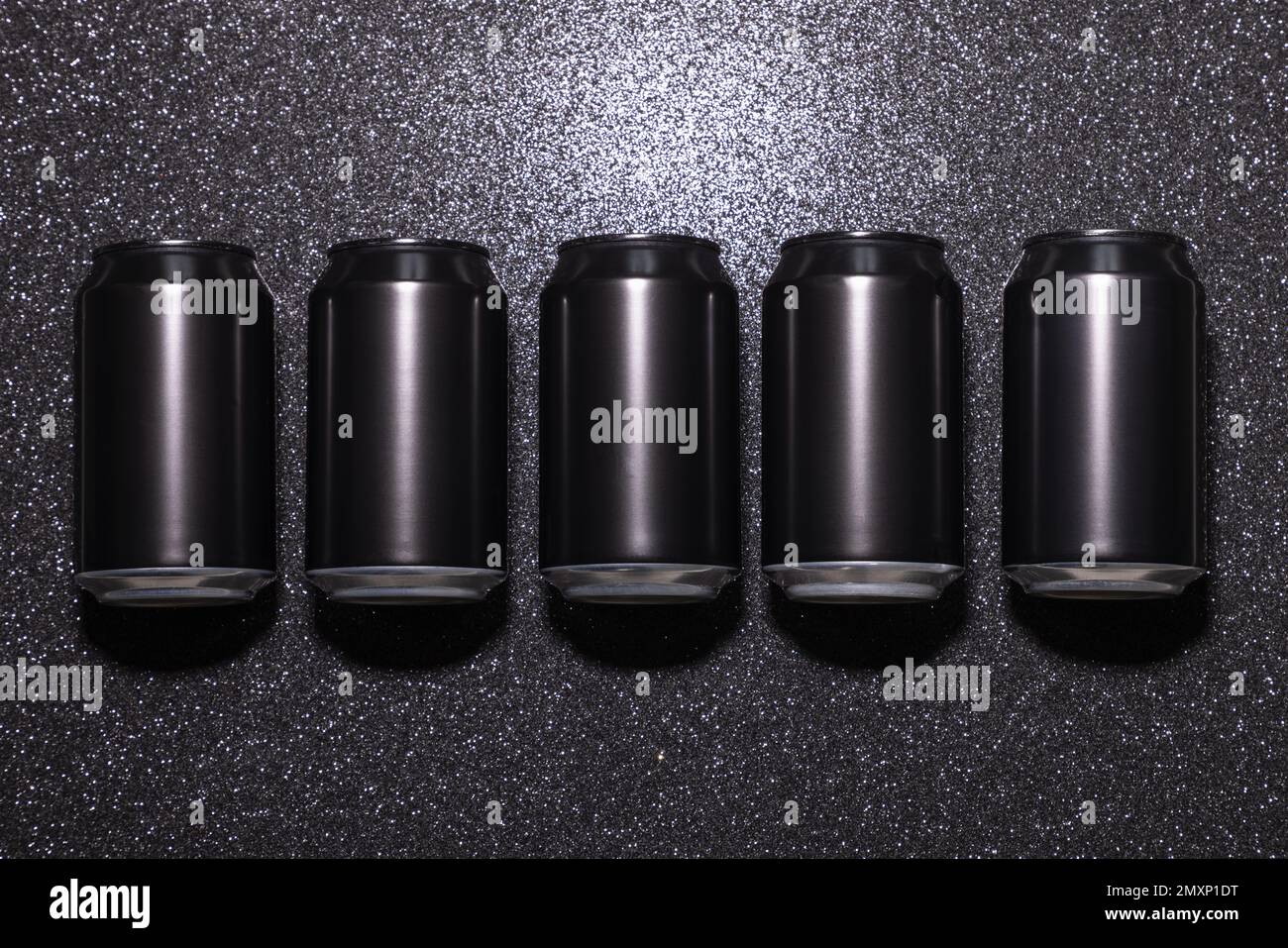 Five black aluminium cans in a row on a black background with glitter ...