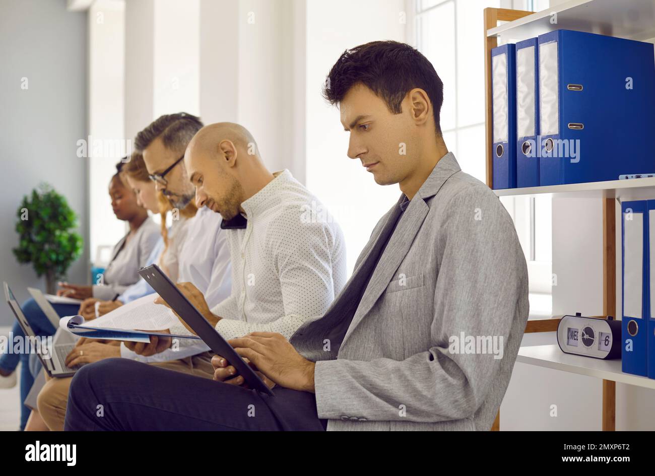Serious man sits with other candidates in waiting room before interview ...